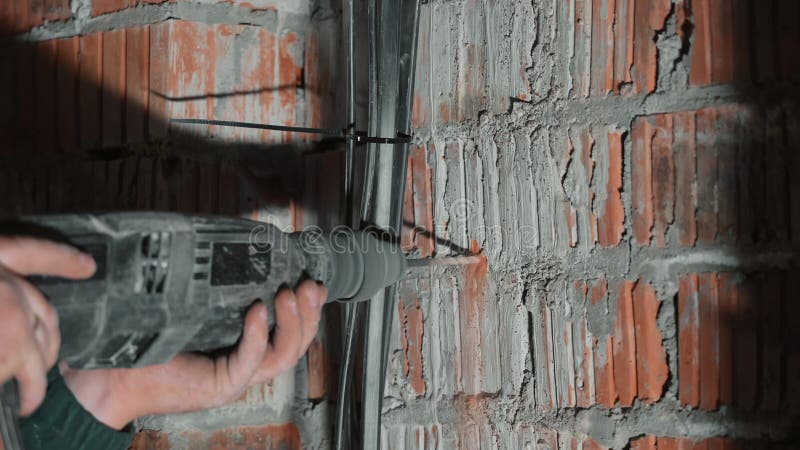Worker Drilling into a Brick Wall To Install Electrical Conduit in a ...