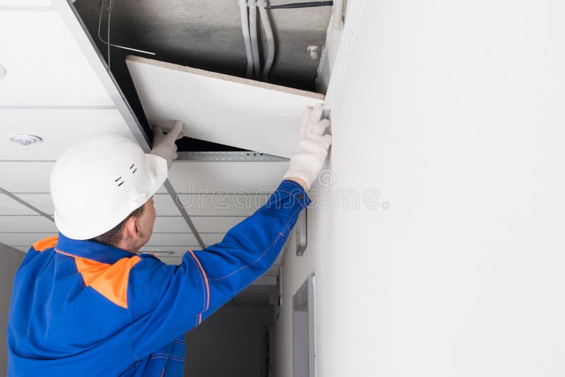 A Worker in a Helmet Repairs a Suspended Ceiling after a Disaster Stock ...