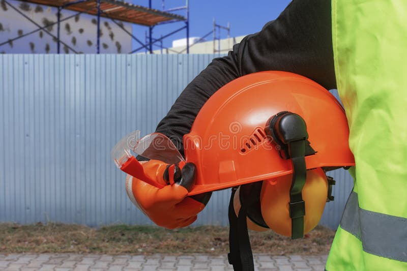 Worker in a High-visibility Vest Holds an Orange Hard Hat with Safety ...