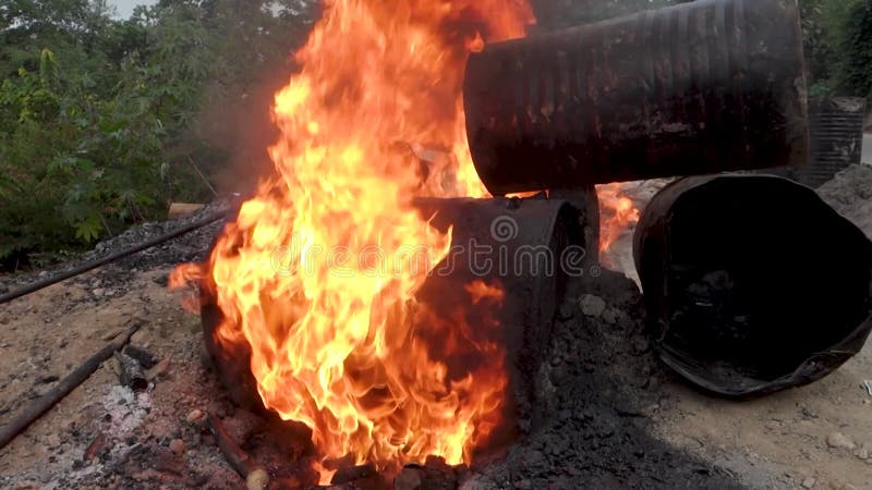 Worker Igniting Charcoal Barrels for Road Construction. Intense Flames ...