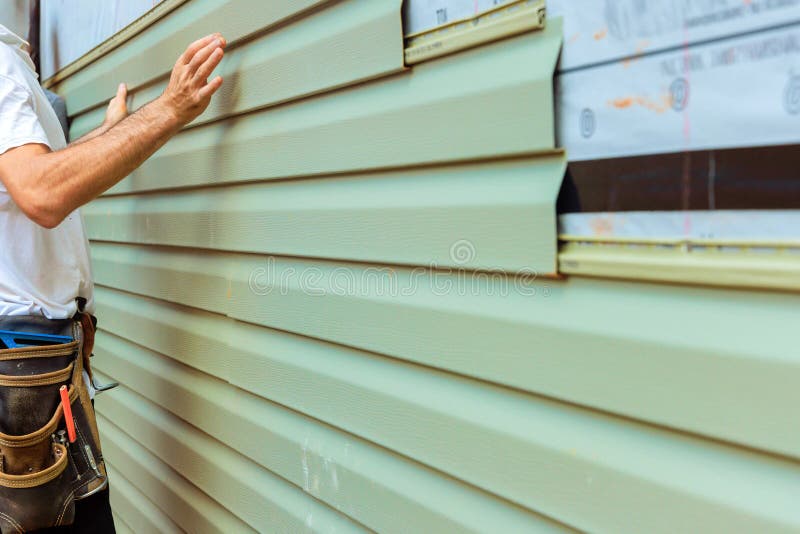 Worker Installing Green Siding on a House while Ensuring Proper ...