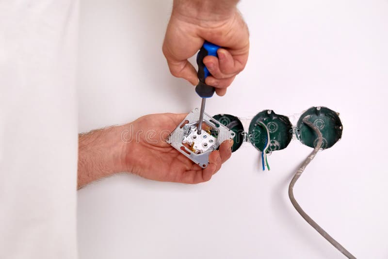 A Worker Installs an Electrical Outlet into a Wall Using a Screwdriver ...