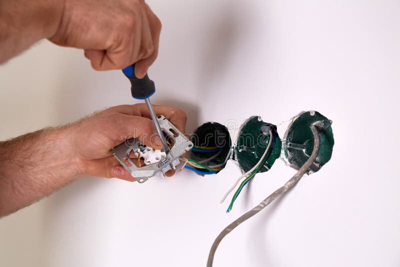 A Worker Installs an Electrical Outlet into a Wall Using a Screwdriver ...