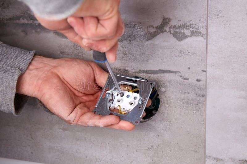 A Worker Installs an Electrical Outlet into a Wall Using a Screwdriver ...