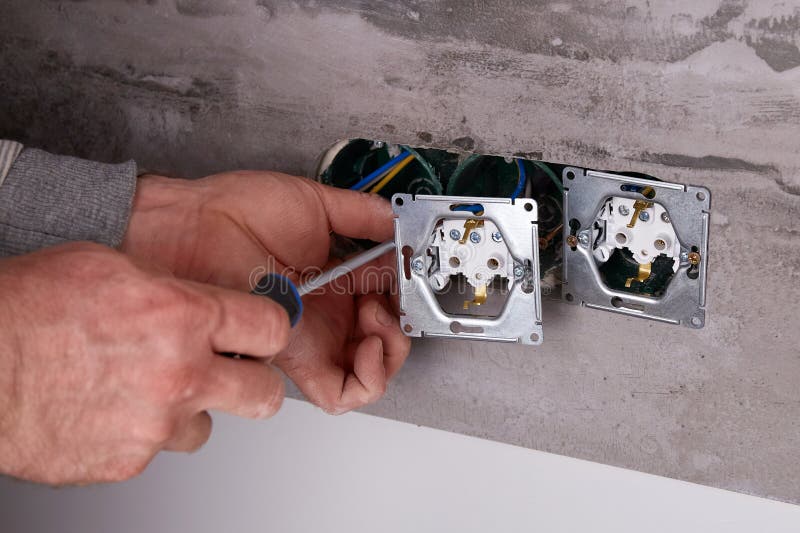 A Worker Installs an Electrical Outlet into a Wall Using a Screwdriver ...
