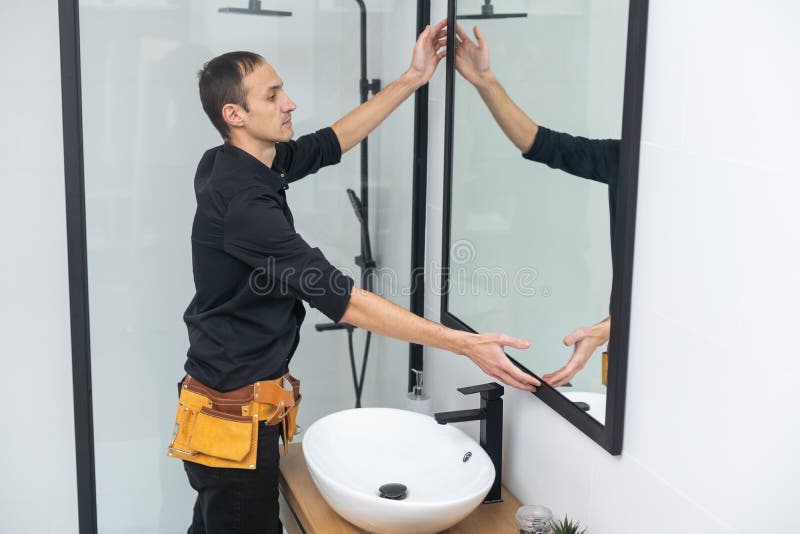 The Worker Installs the Mirror in the Bathroom. Stock Image - Image of ...