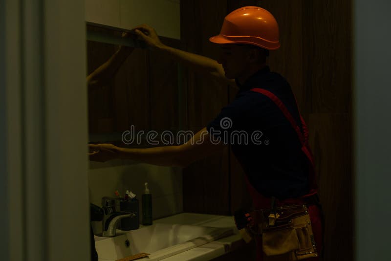 The Worker Installs the Mirror in the Bathroom. Stock Photo - Image of ...