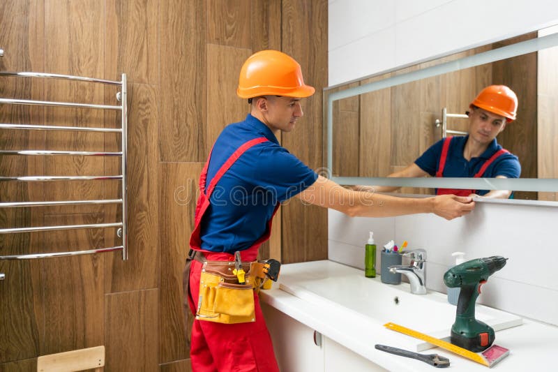 The Worker Installs the Mirror in the Bathroom. Stock Image - Image of ...