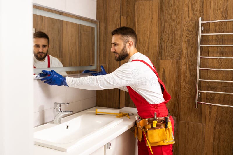 The Worker Installs the Mirror in the Bathroom. Stock Image - Image of ...