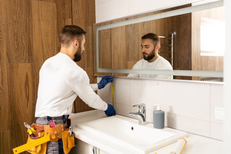 The Worker Installs the Mirror in the Bathroom. Stock Photo - Image of ...