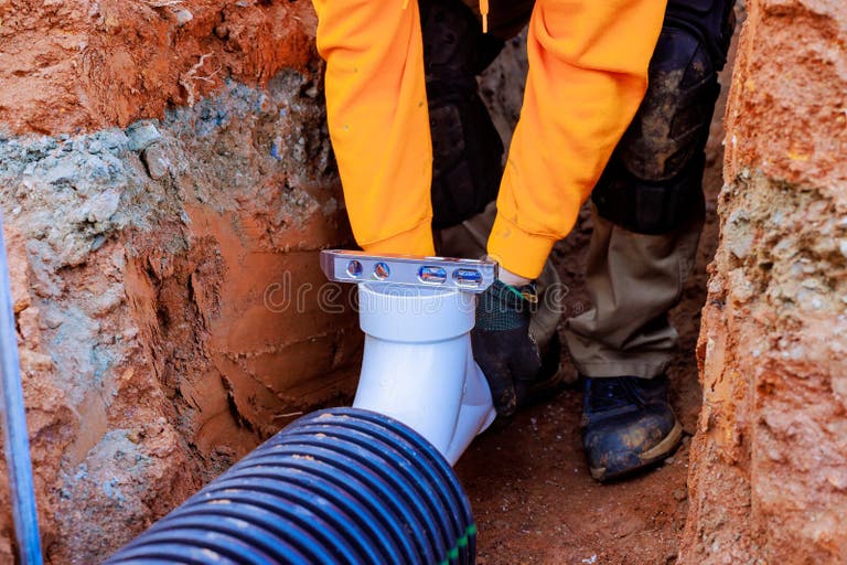 Worker Installs New Drainage Pipe in a Construction Site while Digging ...