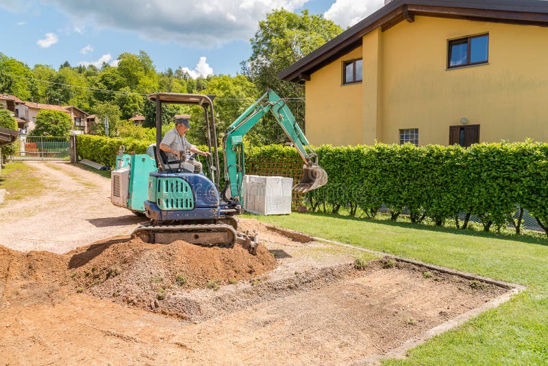 A Worker on a Mini Excavator is Digging the Ground Ahead of the House ...
