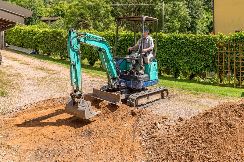 A Worker on a Mini Excavator is Digging the Ground Ahead of the House ...