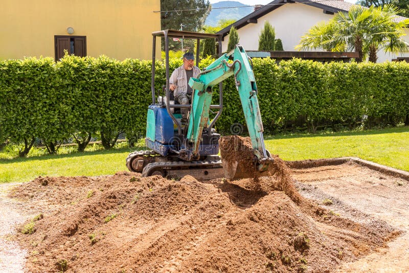 A Worker on a Mini Excavator is Digging the Ground Ahead of the House ...
