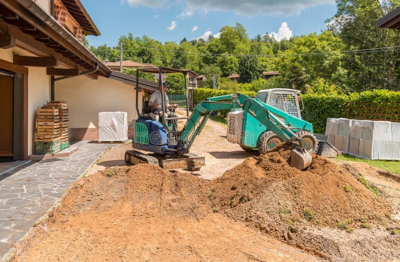 A Worker on a Mini Excavator is Digging the Ground Ahead of the House ...