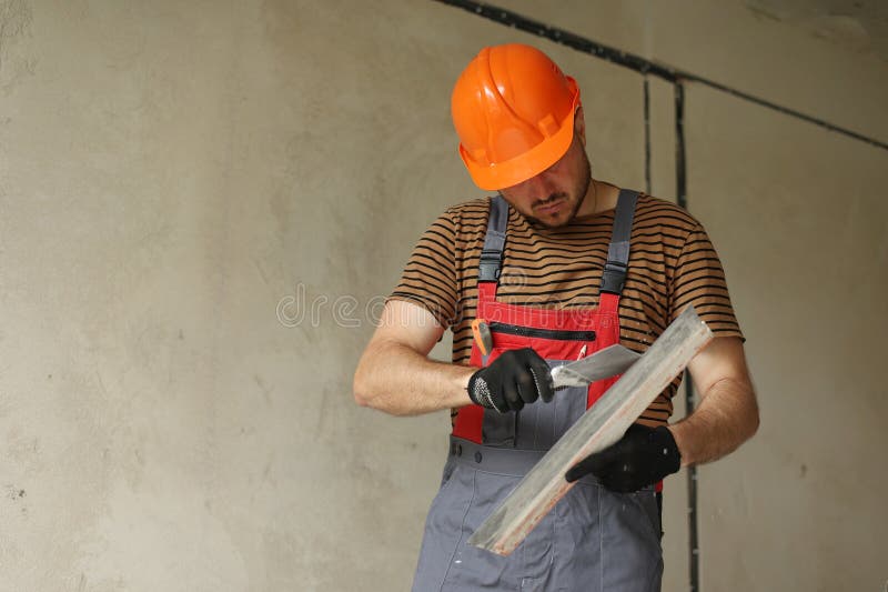 Worker in Overalls and Safety Hard Hat Holds and Prepares Two Spatulas ...