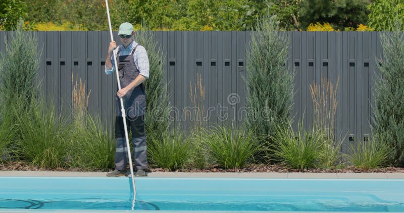 Worker in Overalls Vacuuming the Pool in the Backyard of the House. Top ...