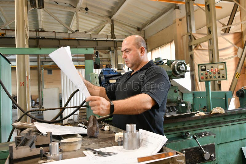 A Worker Reads a Technical Drawing Near a Metalworking Machine before ...