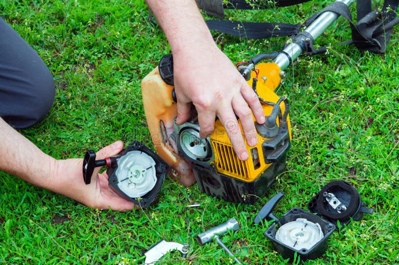 Worker Repairs a Starter in a Trimmer or Lawn Mower that Lies on the ...