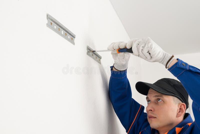 A Worker Screws Fasteners To a White Wall with Self-tapping Screws for ...
