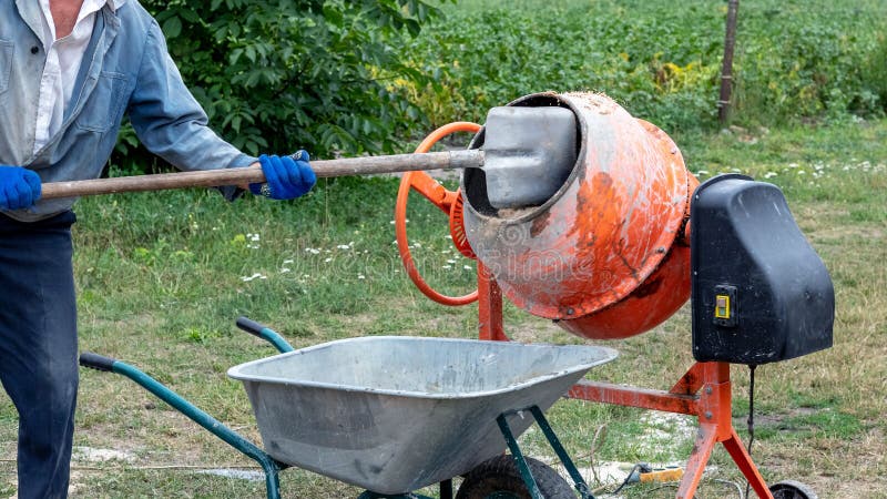 A Worker Shovels Sand into a Concrete Mixer, Preparing Cement Mortar ...