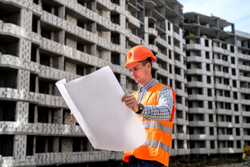 Worker in Uniform and a Helmet Holds in His Hands a Detailed Plan on ...