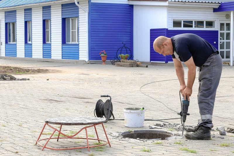 Worker Using a Drill To Perform Maintenance Next To an Open Manhole ...