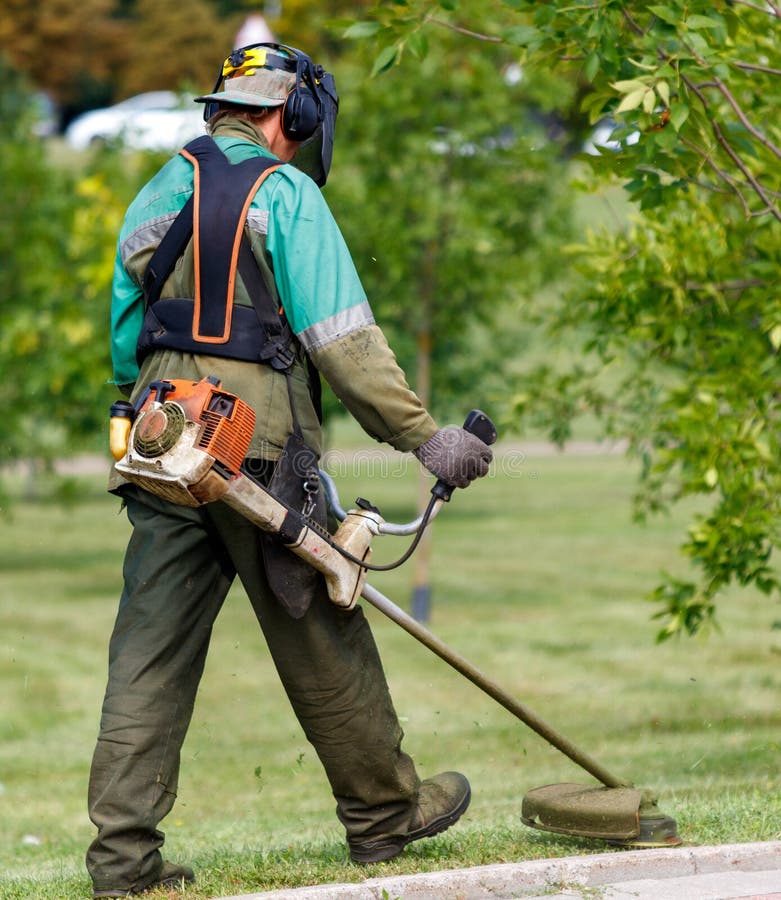 Worker Using a Grass Trimmer To Maintain a Park, Wearing Protective ...