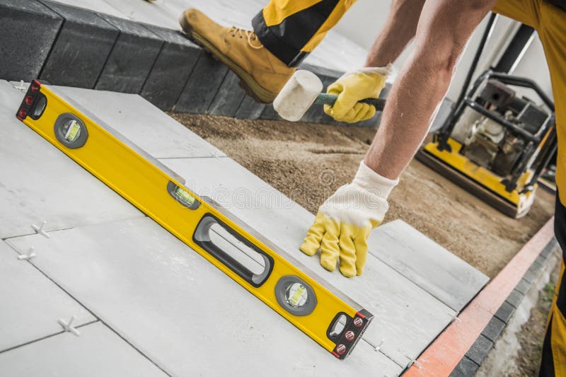 Worker Using a Level Tool To Ensure Evenness while Laying Pavers on a ...