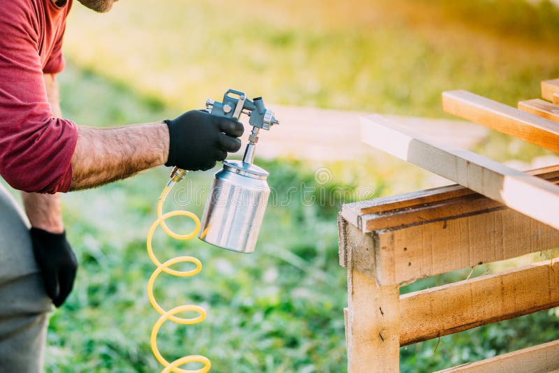 Worker Using Paint Gun or Spray Gun for Applying Paint on Brown Timber ...