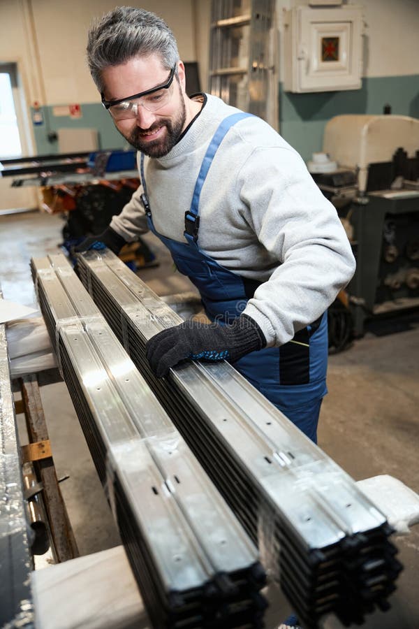 Worker in the Workshop Inspects a Stack of Aluminum Profiles Stock ...