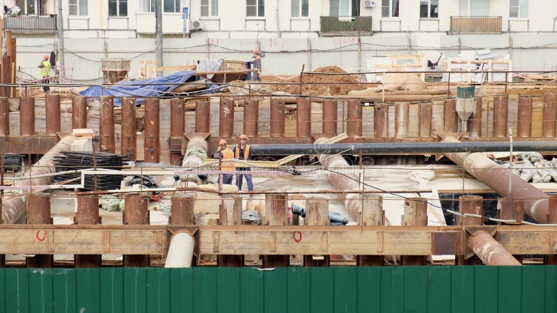 Workers in Helmets and Orange Vests Carry Construction Materials at a ...