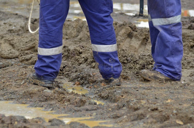 Workers Wearing Overalls and Workboots Stand in a Muddy Environment ...