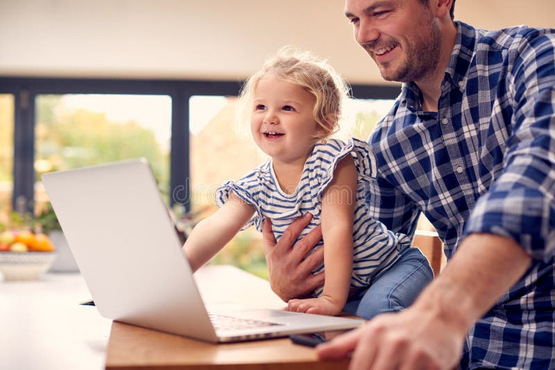 Working Father Using Laptop At Home On Kitchen Counter Whilst Looking ...
