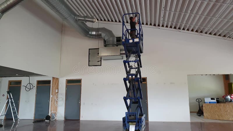 A Working Man on Scissor Lift Fixing Ceiling. Construction Work Concept ...