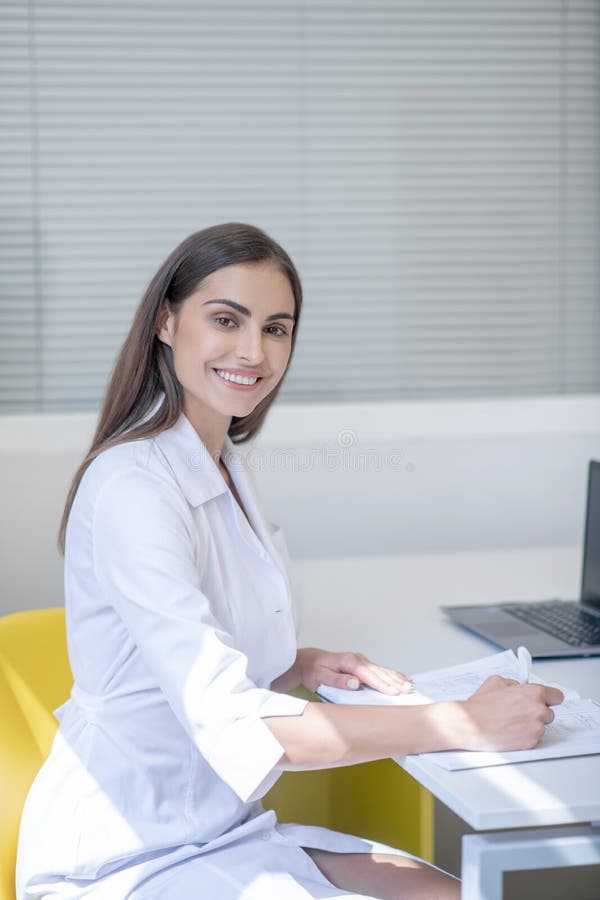 Pretty Doctor in a Lab Coat Smiling and Making Notes Stock Photo ...