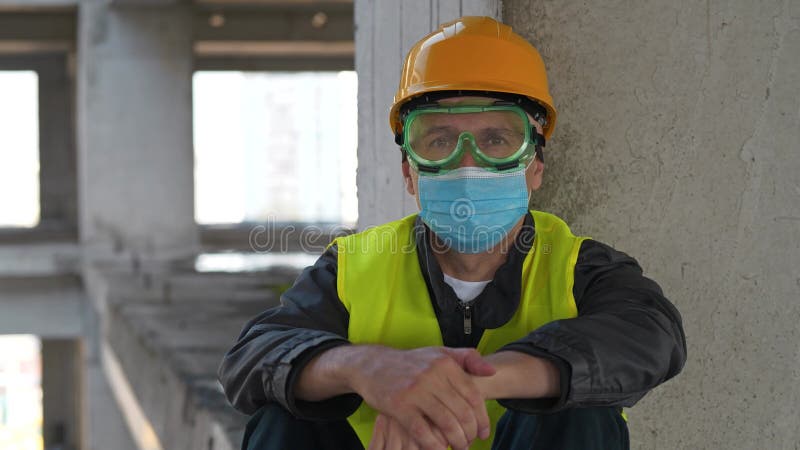Workman in Protective Face Mask Sits at Construction Site and Looks at ...