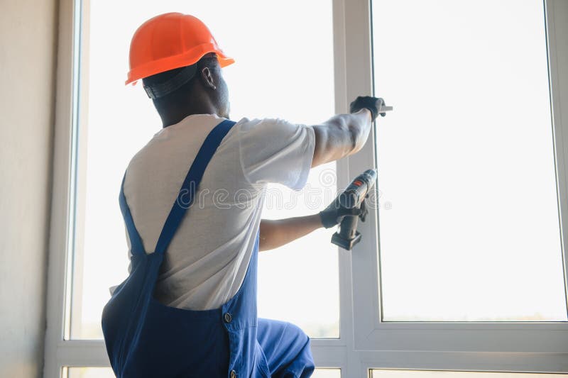 African Workman in Overalls Installing or Adjusting Plastic Windows in ...