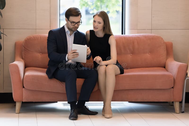 Workmates Using Digital Tablet Working Seated on Sofa in Workspace ...