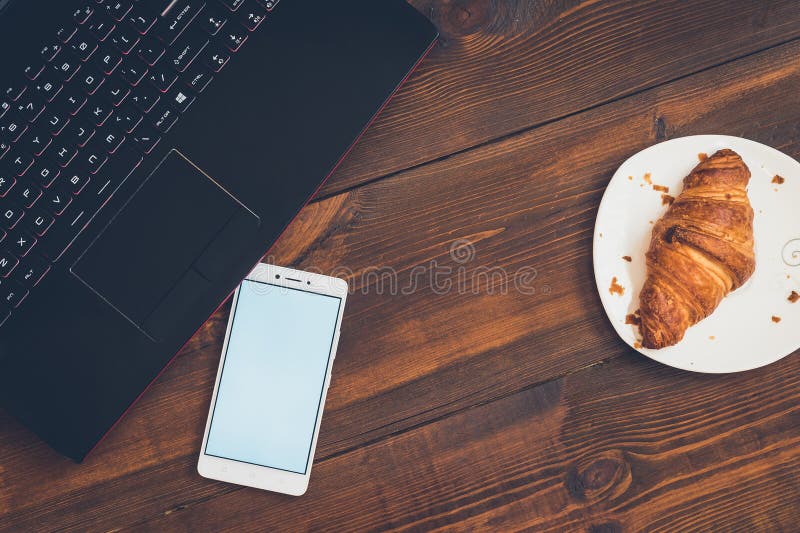 Workspace with Laptop, Smartphone and Croissant on Wooden Desk Stock ...