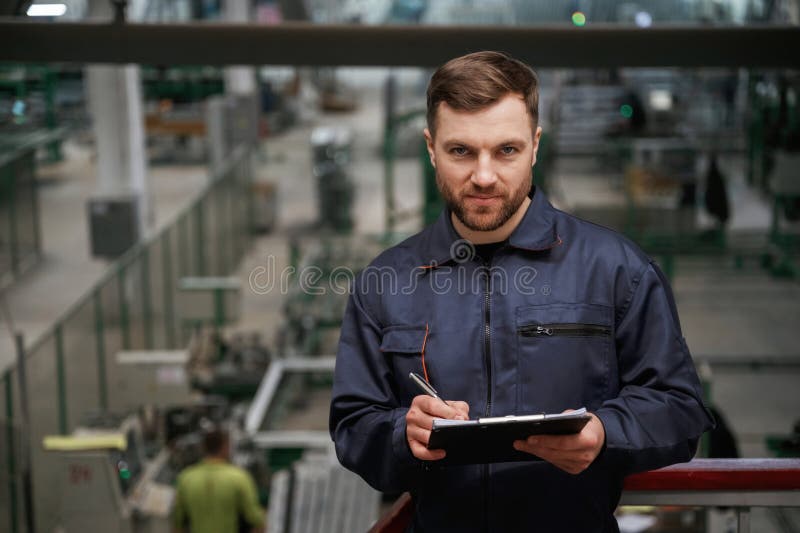 Writing Information into the Notepad. Factory Worker is Indoors with ...