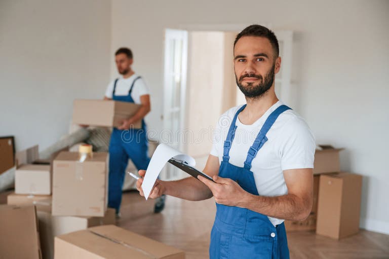 Writing in Notepad, Holding Box. Two Moving Service Employees in a Room ...