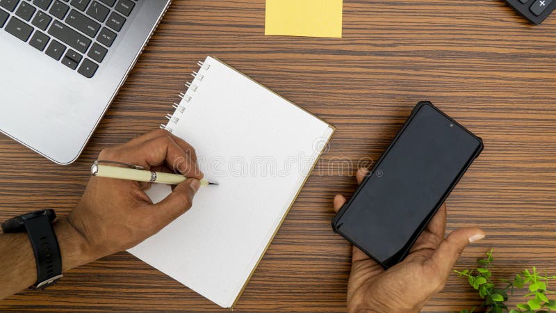 Writing on a Notepad while Holding a Mobile Phone Working in an Office ...