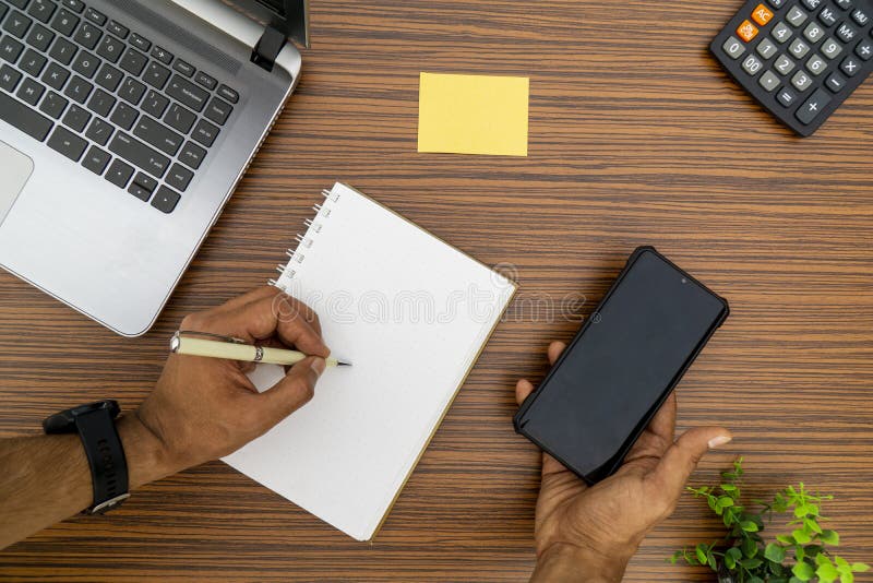 Writing on a Notepad while Holding a Mobile Phone Working in an Office ...
