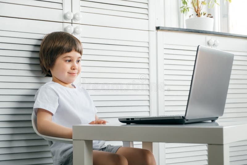 5 Year Boy Sit at the Table Uses Laptop and Looks at the Screen. Child ...