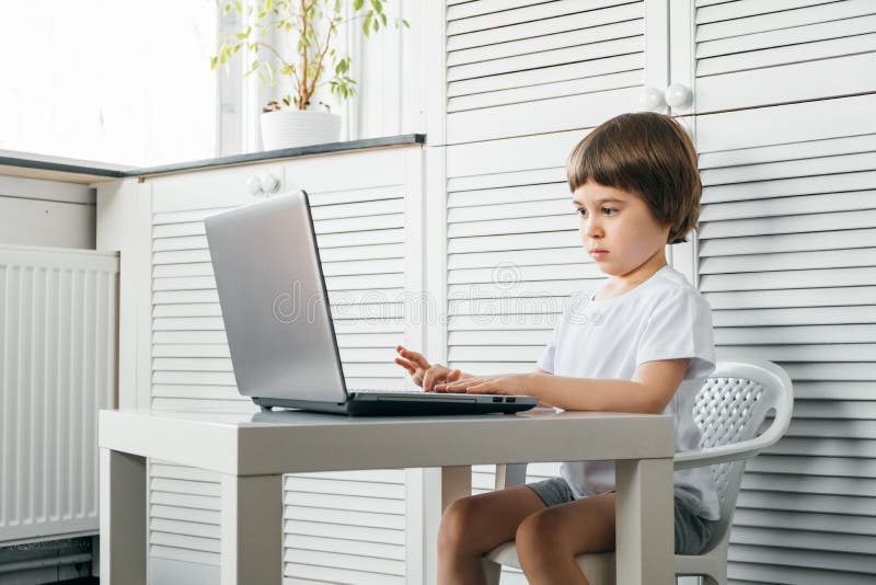 5 Year Boy Sit at the Table Uses Laptop and Looks at the Screen. Child ...