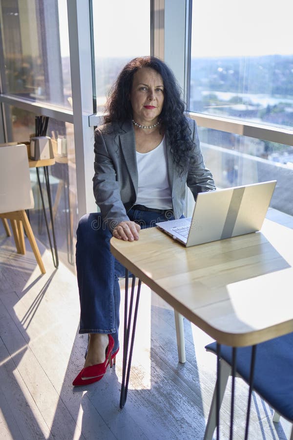 A 57-year-old Woman Works on a Laptop in a Modern Office Workspace ...