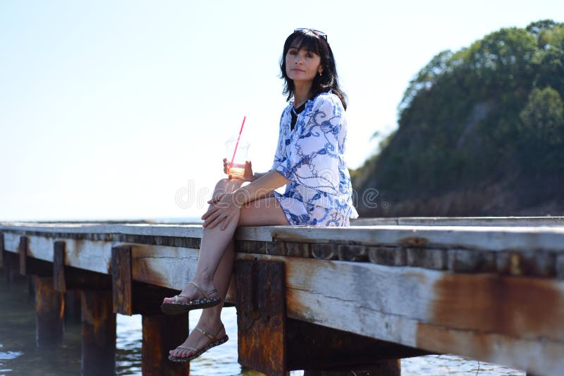 45 Years Old Russian Woman Drinking Lemonade And Sitting On Pier Stock