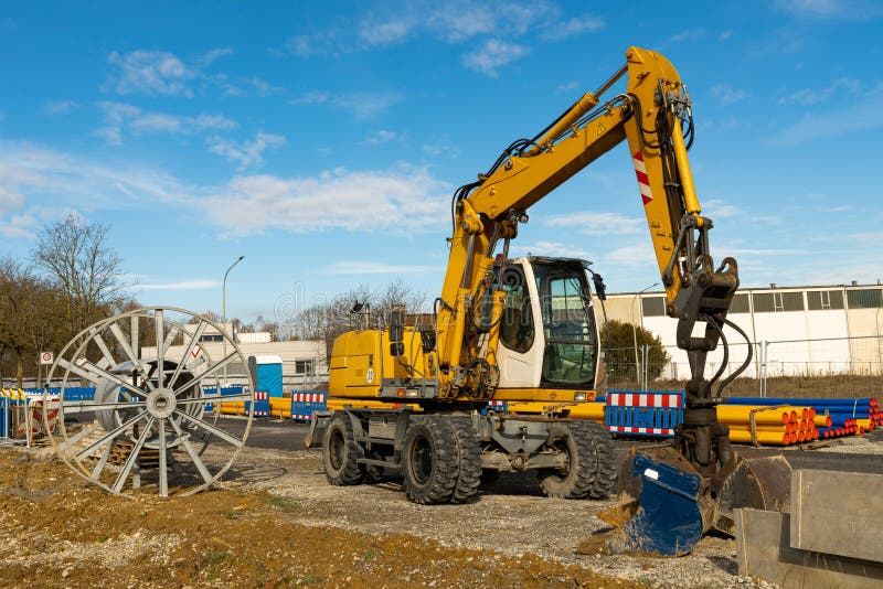 Yellow Excavator at a Construction Site Next To an Empty Cable Drum ...