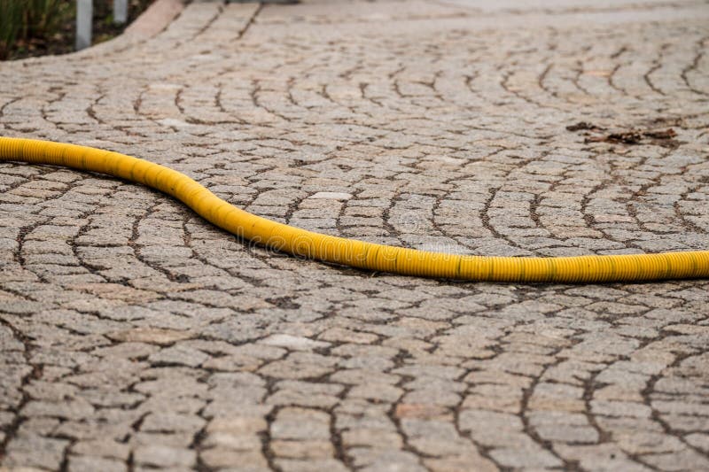 Yellow Flexible Hose on Cobblestone Pavement.. Stock Image - Image of ...